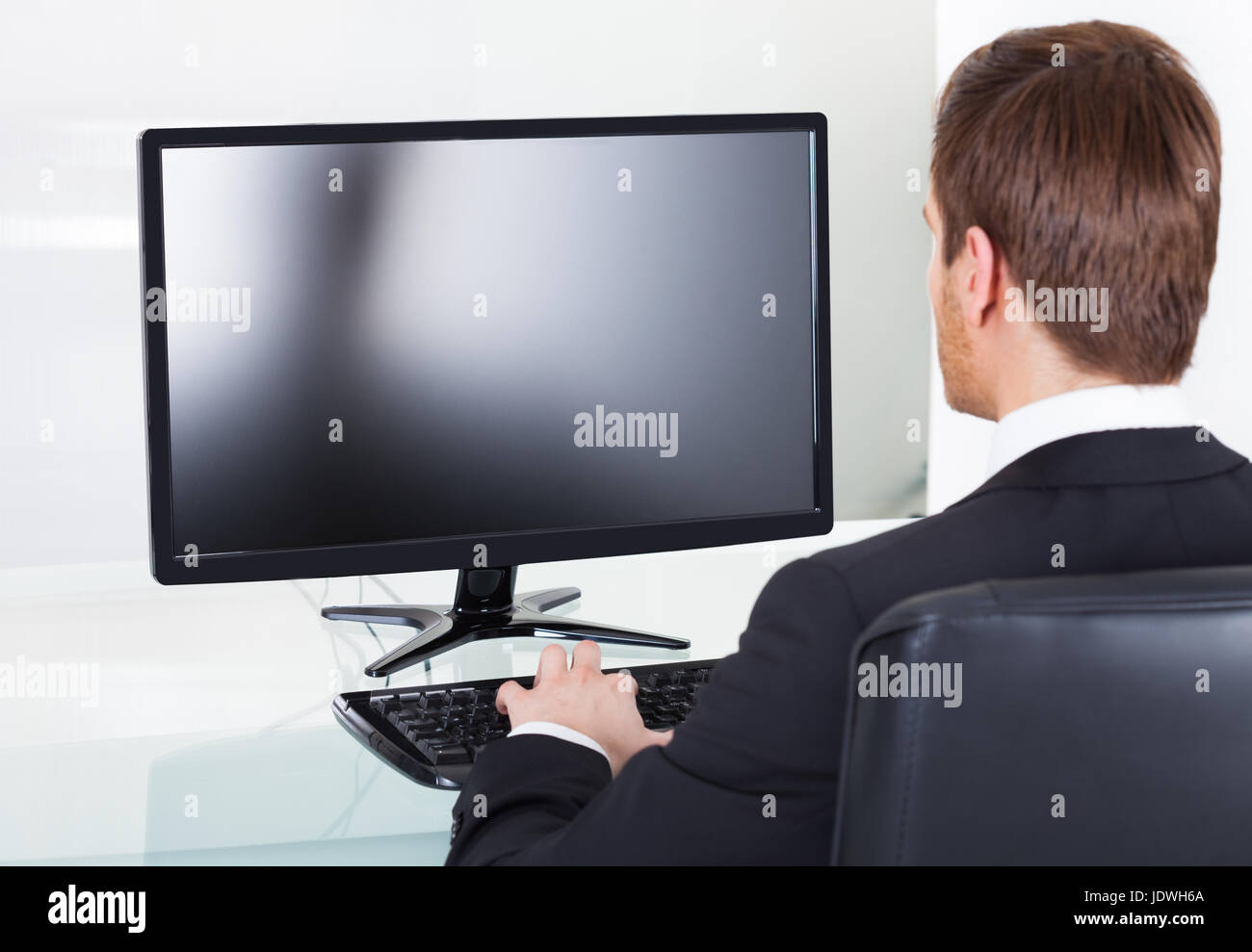 Rear view of young businessman using computer at desk in office Stock ...