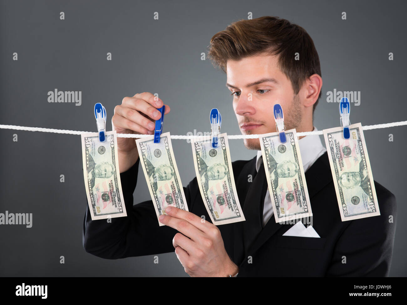 Young businessman drying dollar bills on clothesline against gray ...
