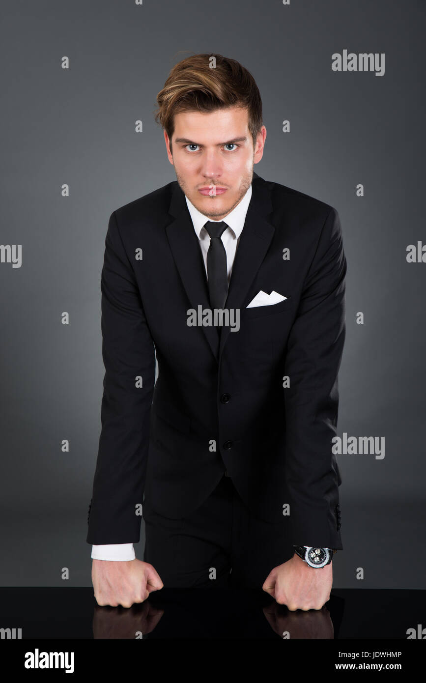 Portrait of angry businessman leaning on table isolated over gray ...