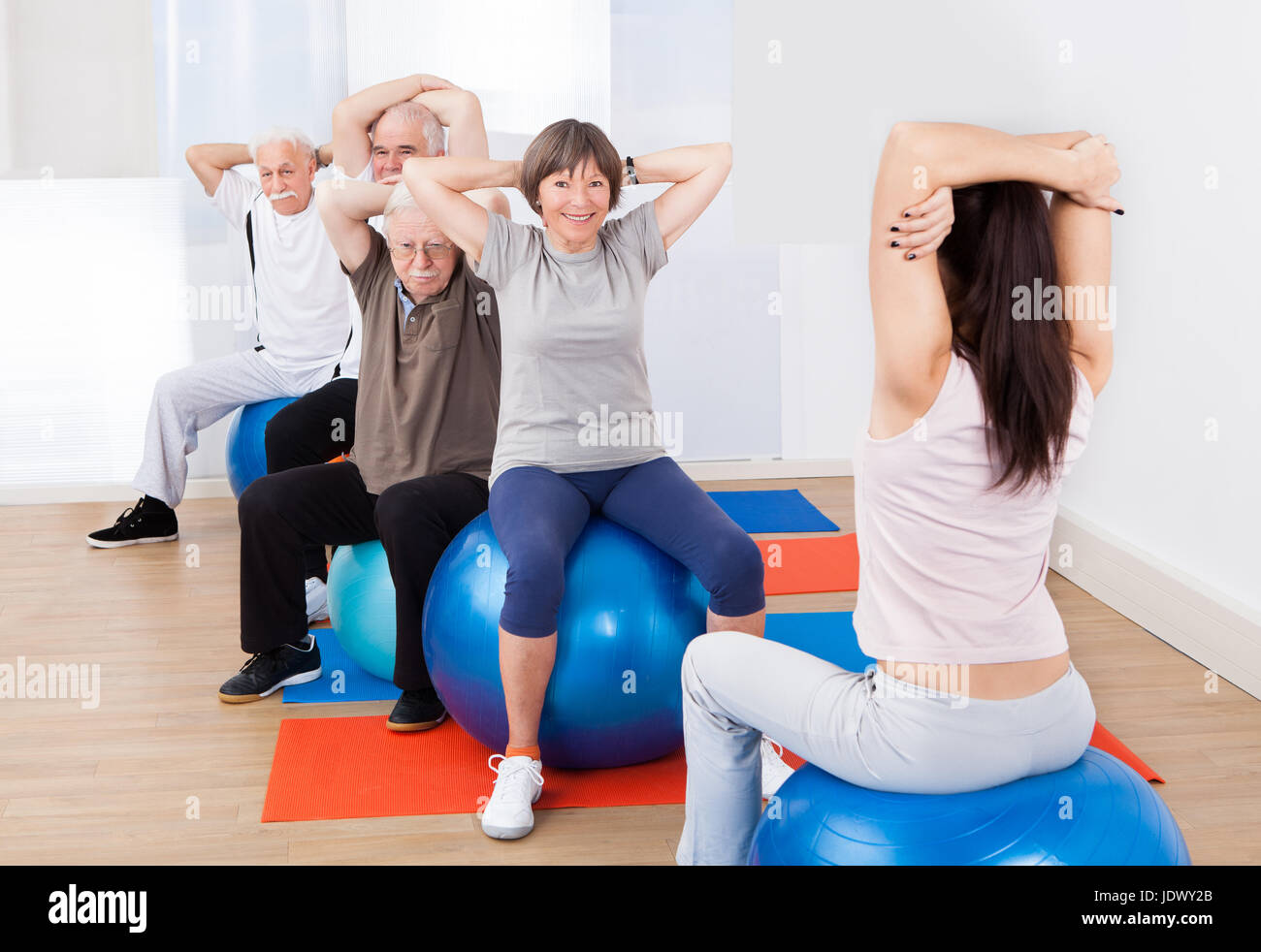 Rear view of female trainer training senior customers stretching on ...