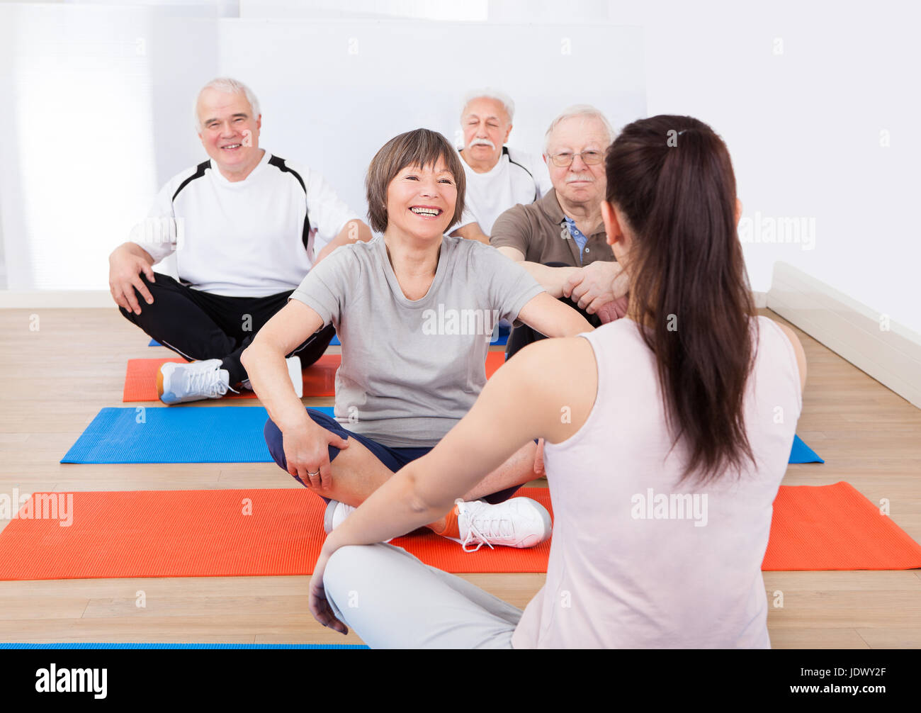 Rear view of female trainer training senior customers on floor in yoga ...