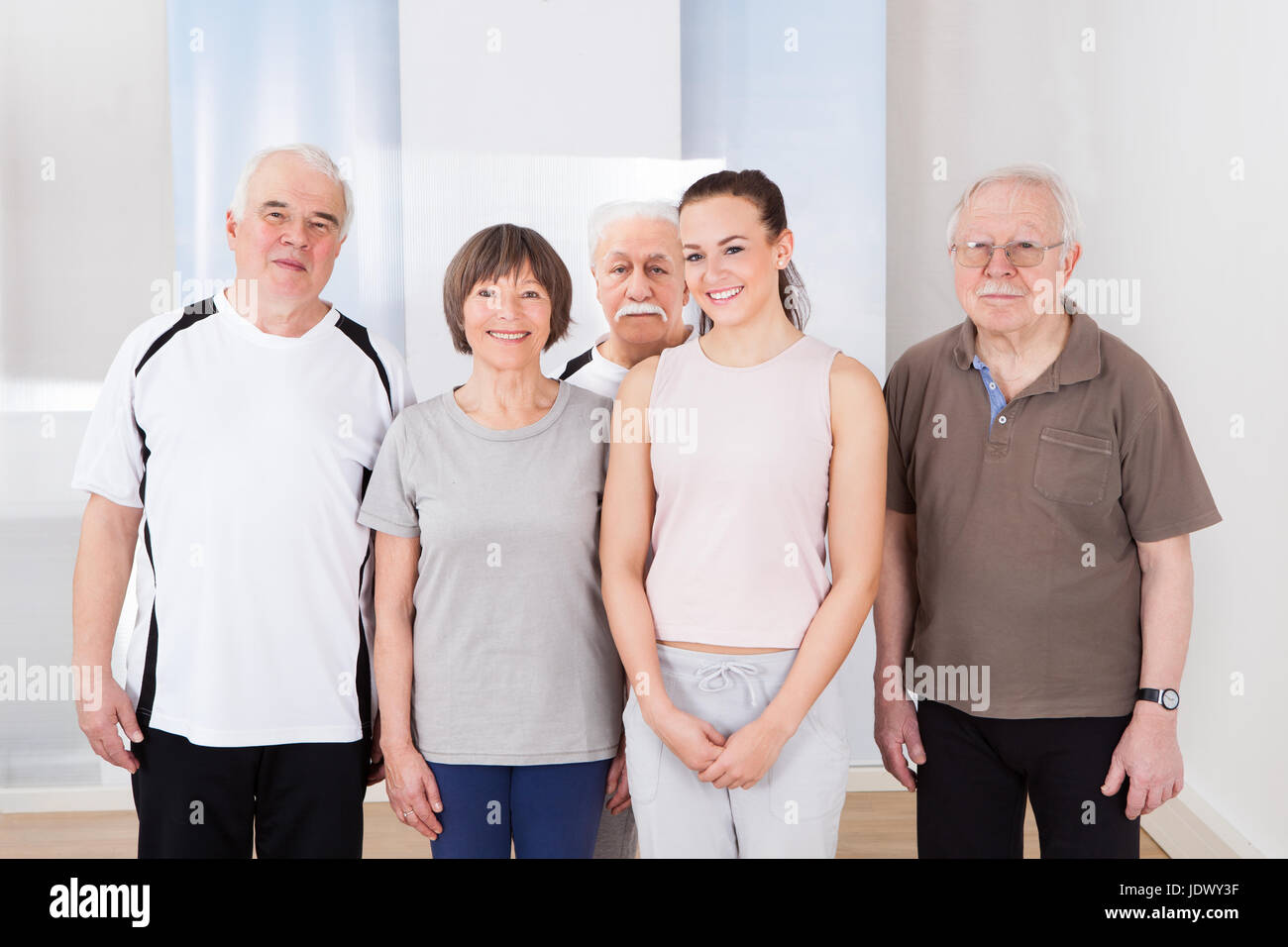 Full length portrait of confident trainer and senior customers standing ...