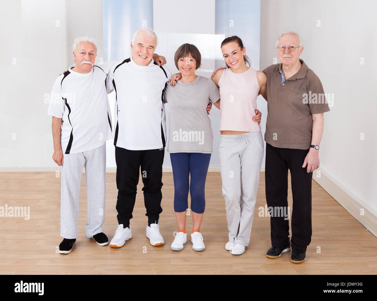 Full length portrait of confident trainer and senior customers standing ...