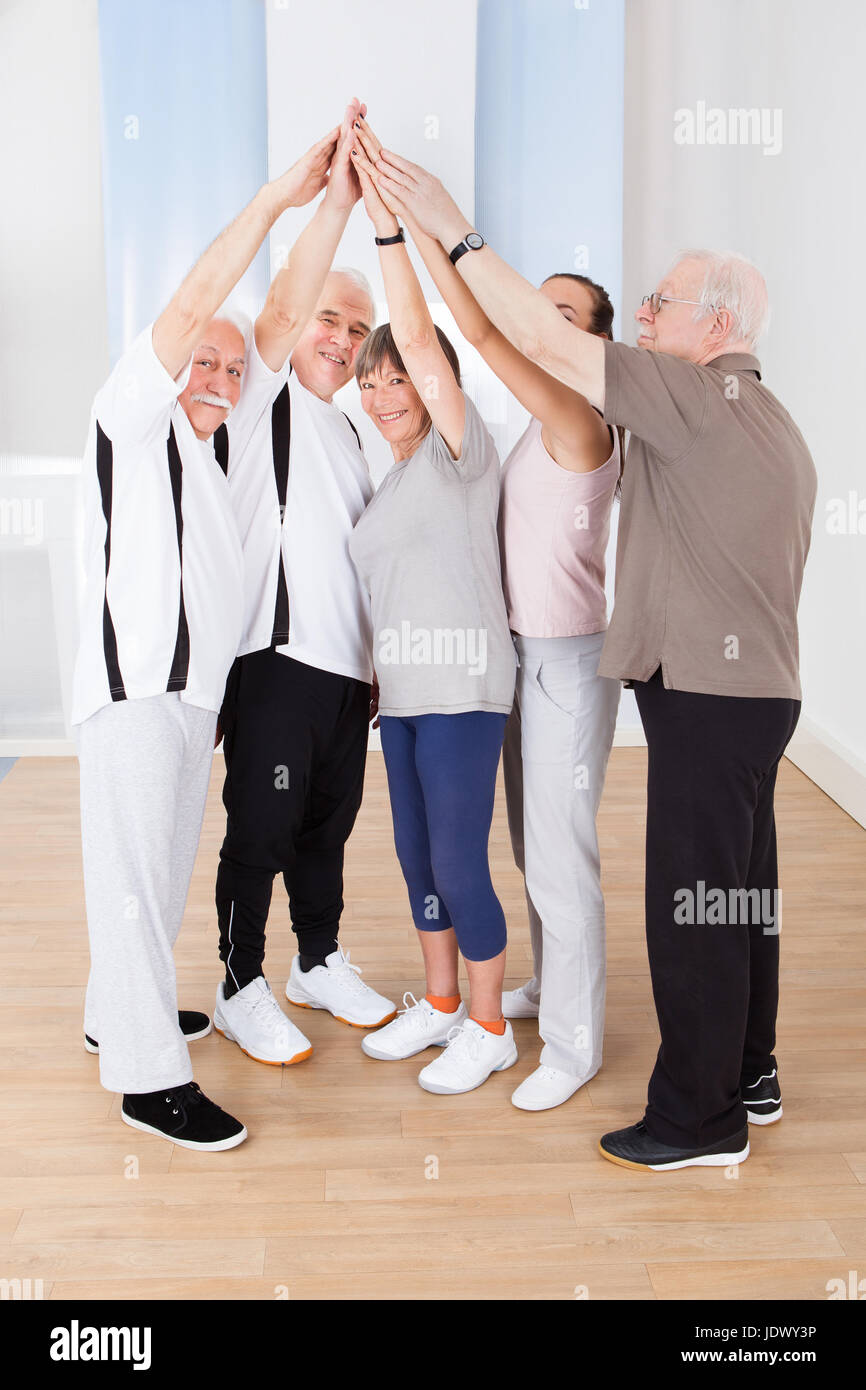 Full length portrait of trainer and senior customers joining hands ...