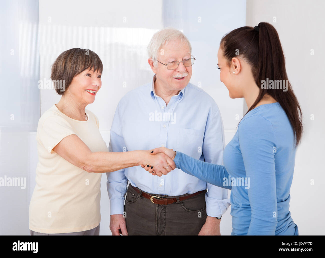 Young female caregiver shaking hands with senior couple at nursing home ...