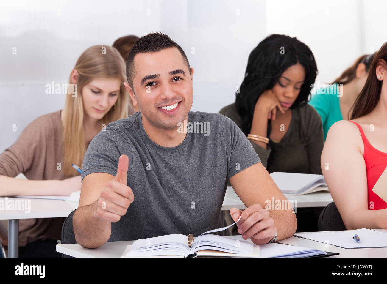 Portrait of confident male college student sitting at desk with ...