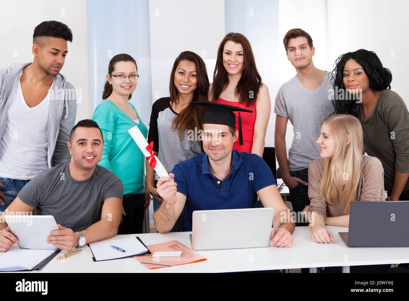 Portrait of college student holding degree with classmates looking at ...