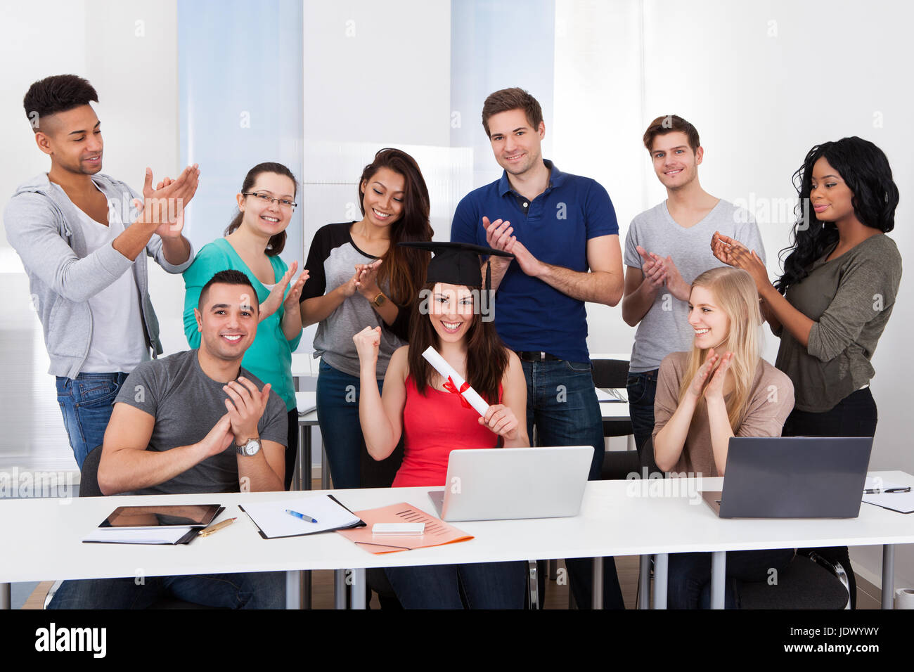 University students clapping for classmate holding degree in classroom ...