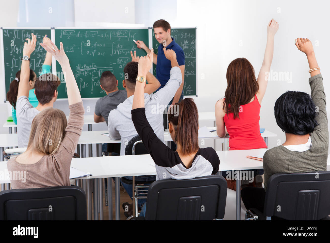 University students with arms raised answering teacher in mathematics ...