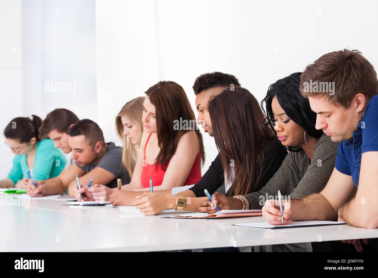 Row of multiethnic college students writing at desk in classroom Stock ...