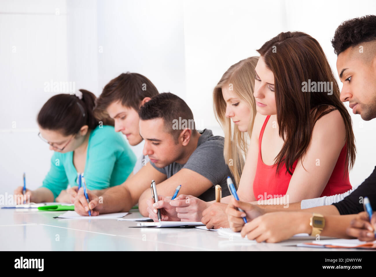 Row of multiethnic college students writing at desk in classroom Stock ...