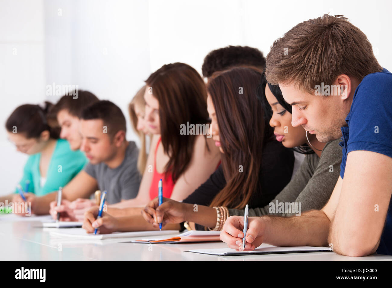 Row of multiethnic college students writing at desk in classroom Stock ...