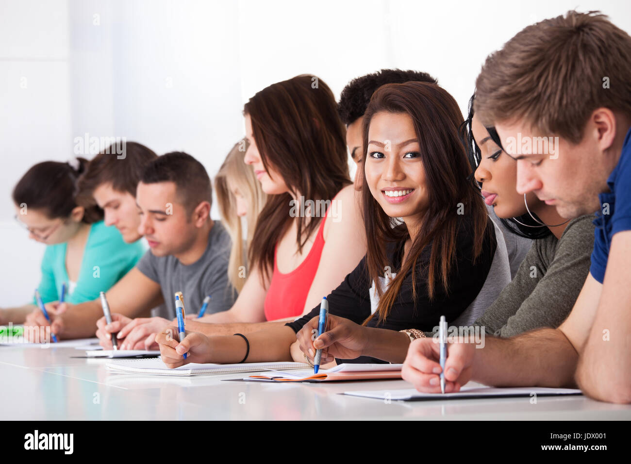 Portrait of smiling college student sitting with classmates writing at ...