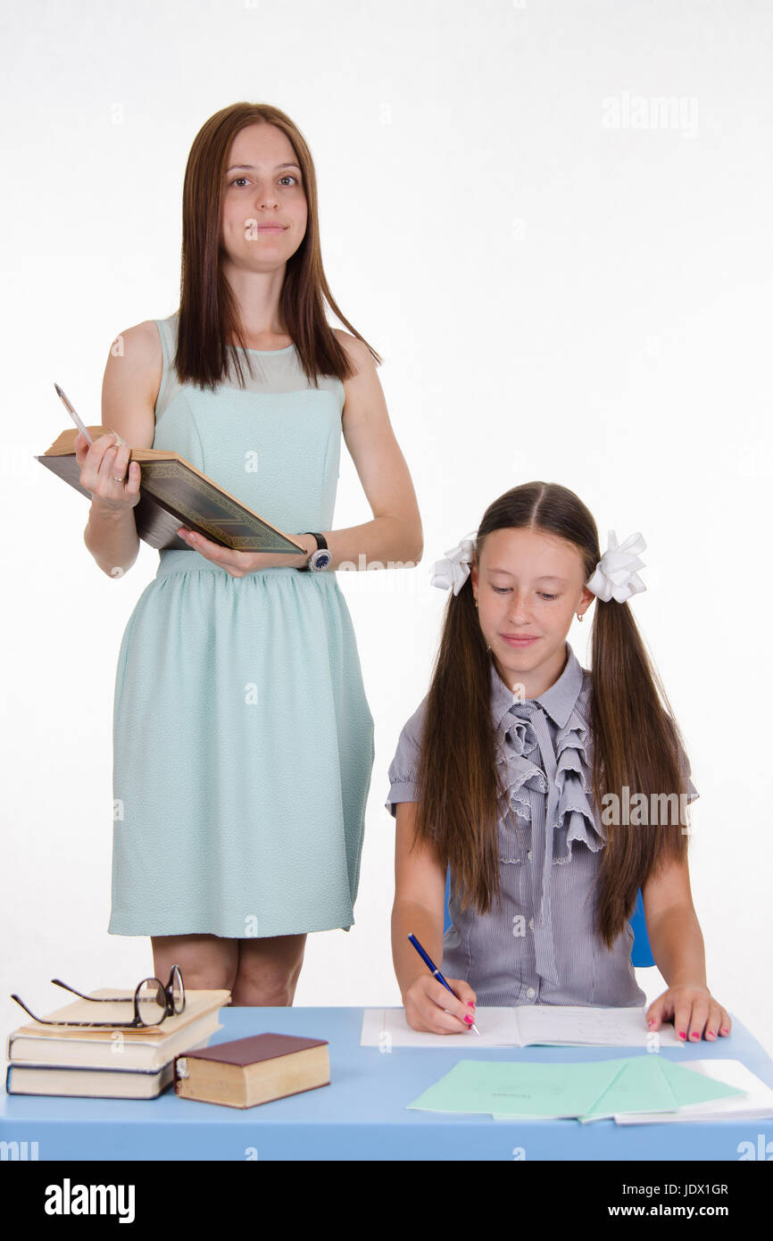Teacher standing at desk behind which sits a diligent student Stock ...