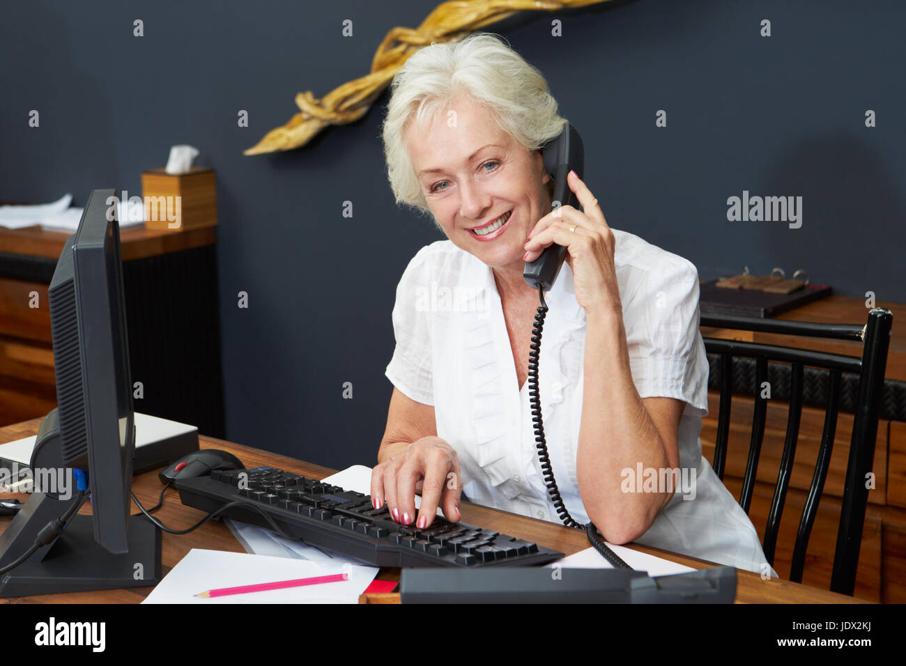 Hotel Receptionist Using Computer And Phone Stock Photo - Alamy