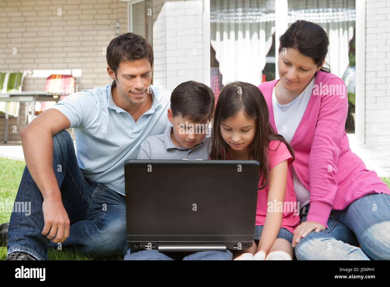 Happy young family sitting outside their house using laptop Stock Photo ...