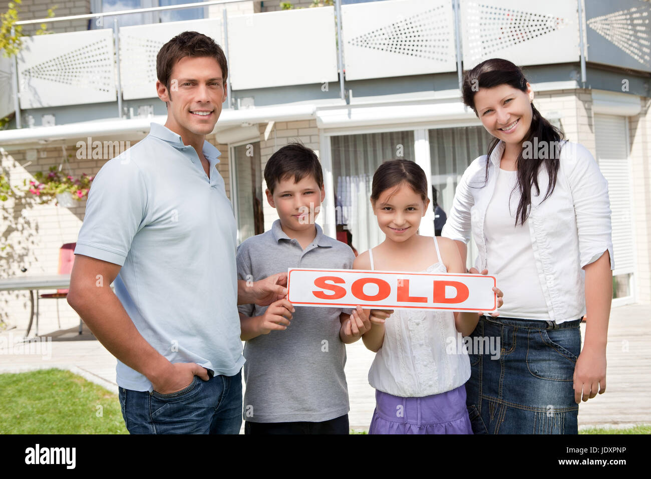 Smiling young family with a sold sign standing outside their new house ...