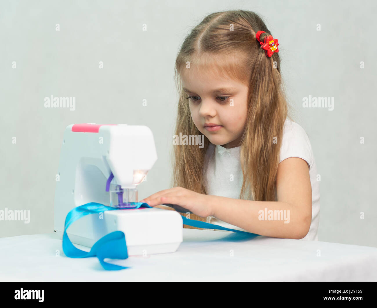 Girl sew on a children's sewing machine. Studio, a white background ...