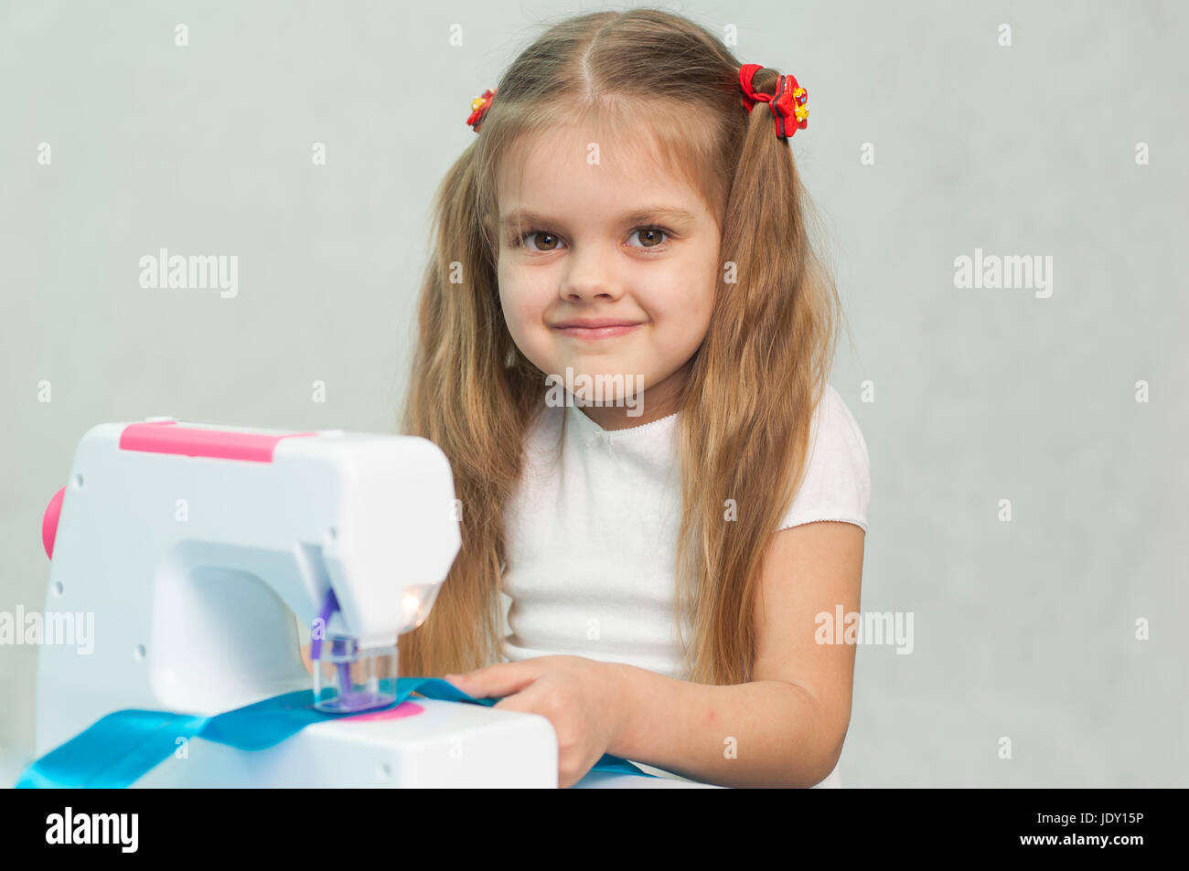 Girl sew on a children's sewing machine. Studio, a white background ...