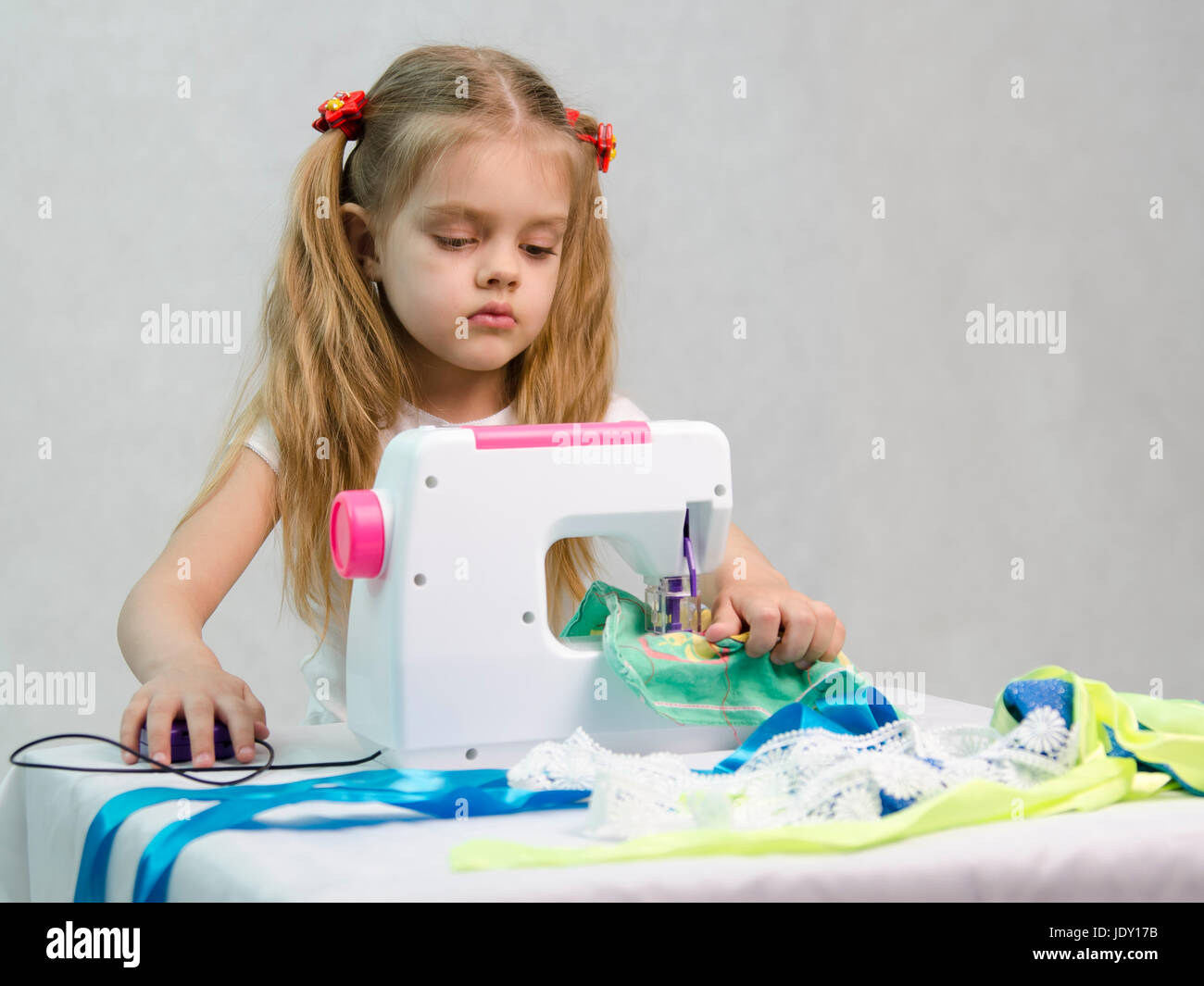 Girl sew on a children's sewing machine. Studio, a white background ...