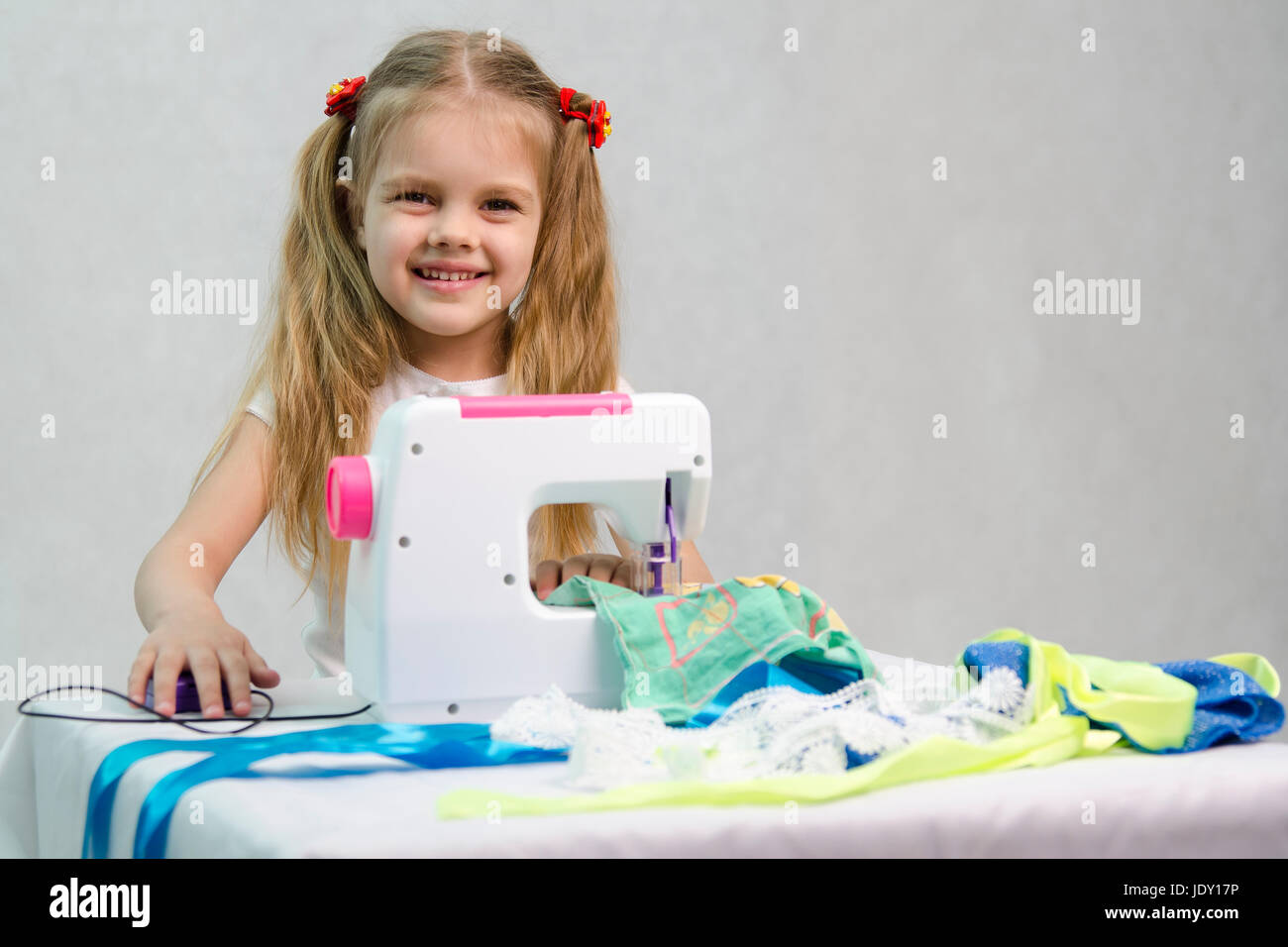 Girl sew on a children's sewing machine. Studio, a white background ...