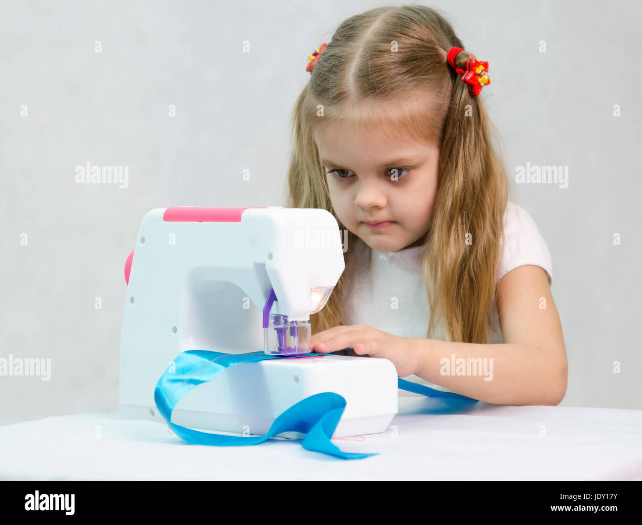 Girl sew on a children's sewing machine. Studio, a white background ...