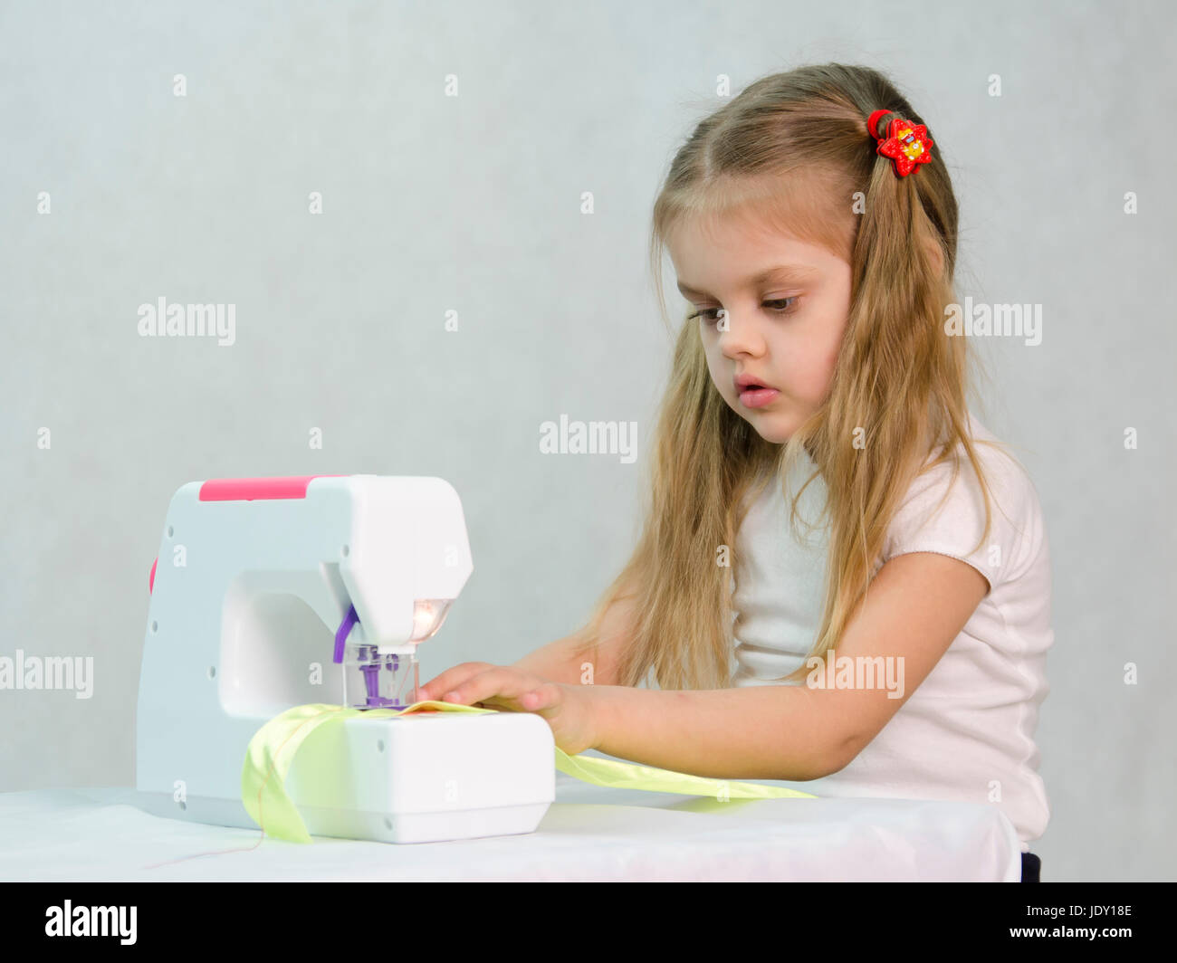 Girl sew on a children's sewing machine. Studio, a white background ...