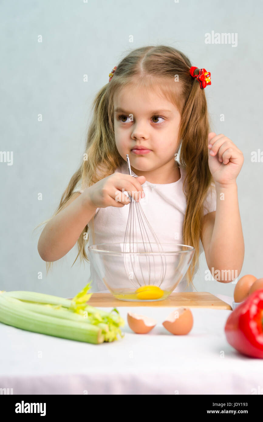 Girl playing in a cook. Girl churn whisk the eggs in a glass bowl. At ...