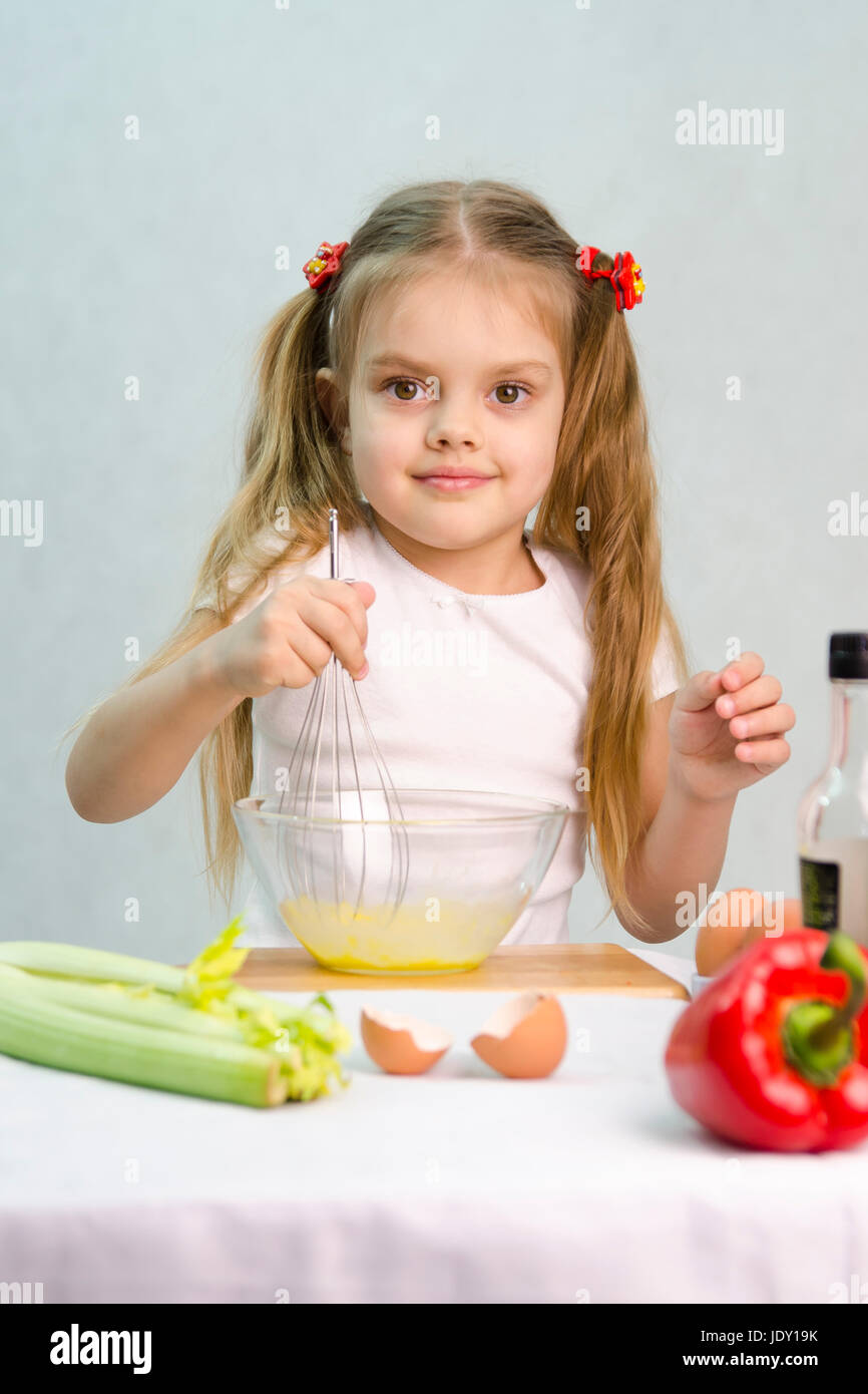 Girl playing in a cook. Girl churn whisk the eggs in a glass bowl. At ...