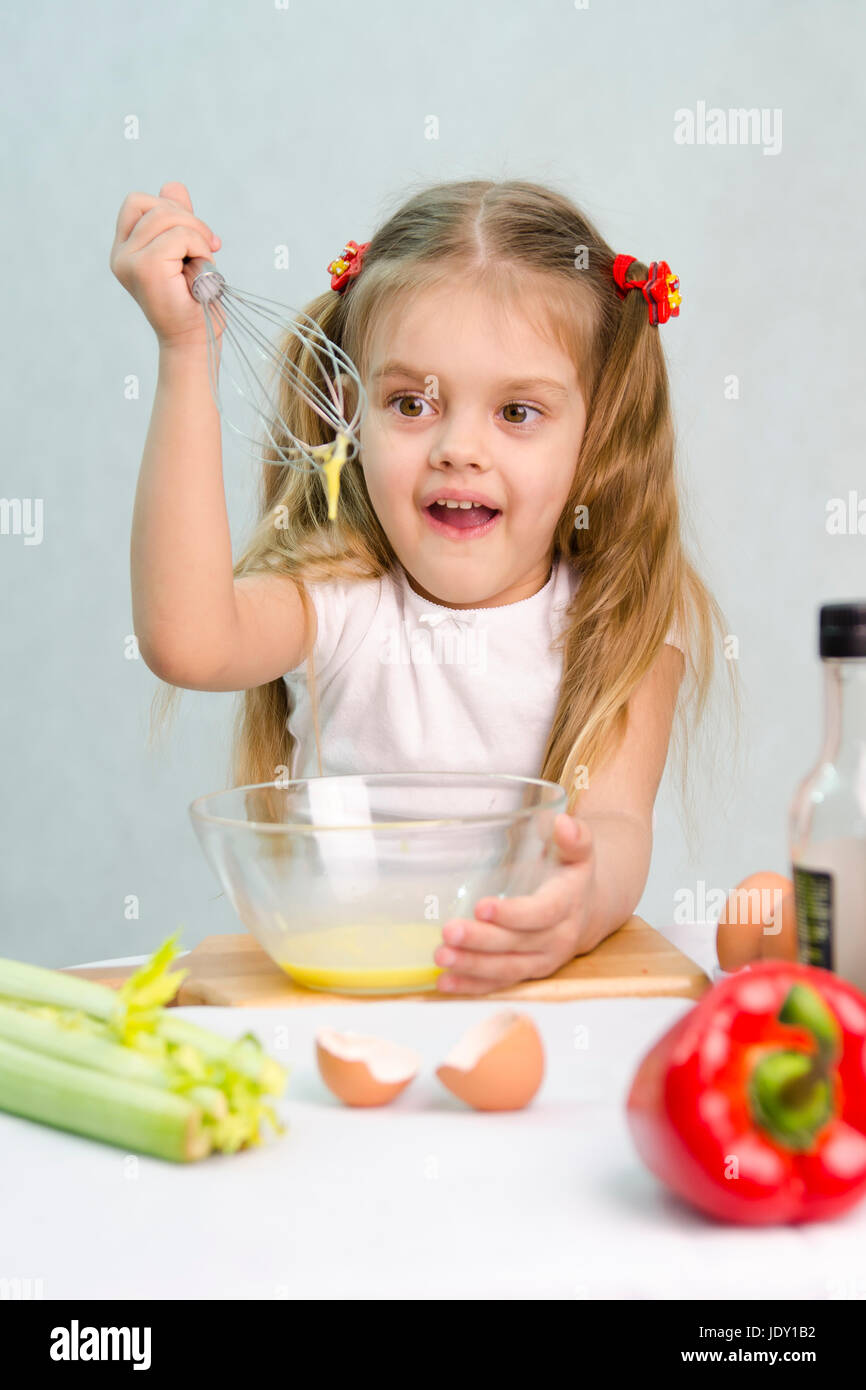 Girl playing in a cook. Girl churn whisk the eggs in a glass bowl. At ...