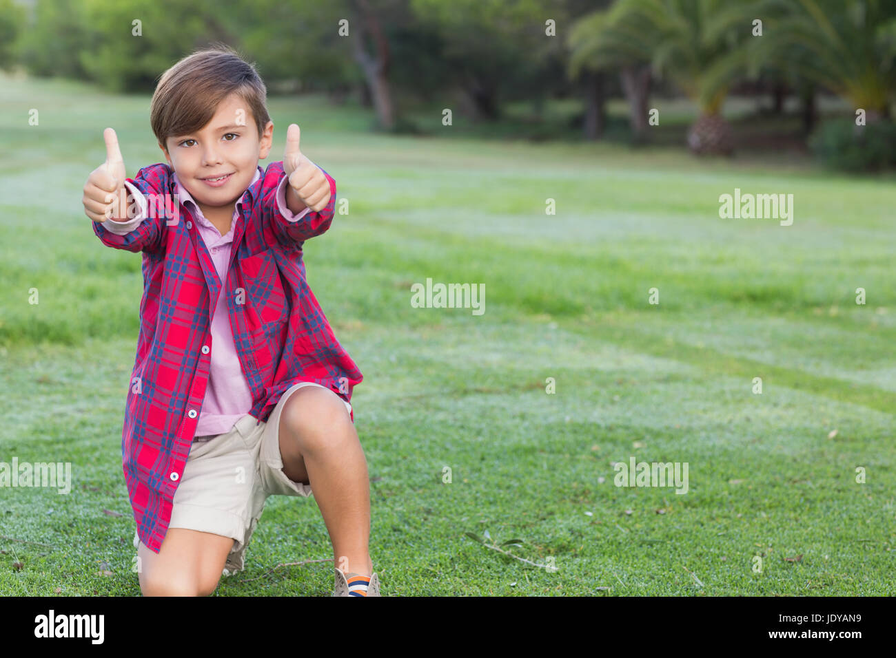 Cute boy kneeling in the park giving thumbs up Stock Photo - Alamy