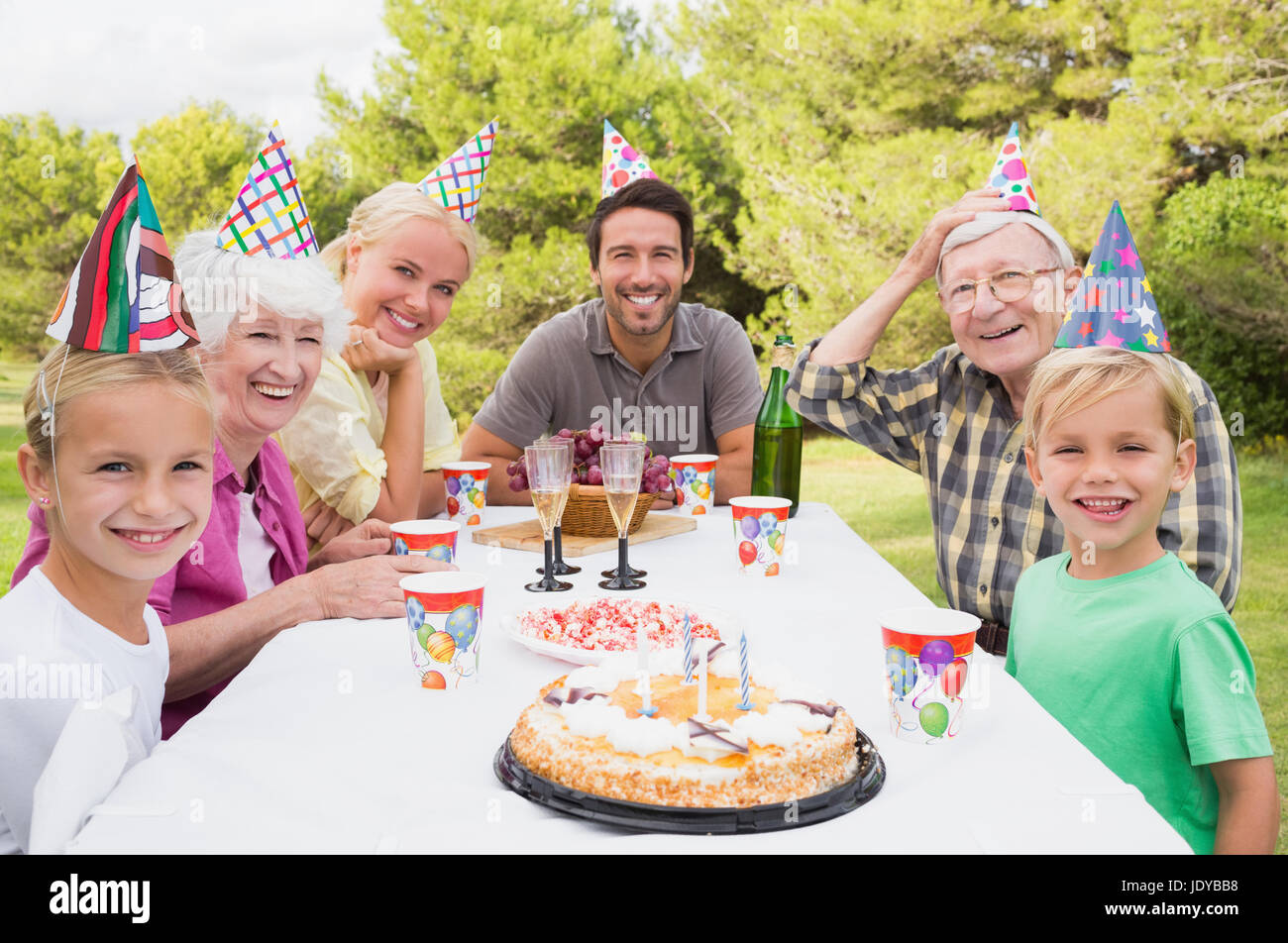 Multi-generation family having a birthday party sitting at picnic table ...