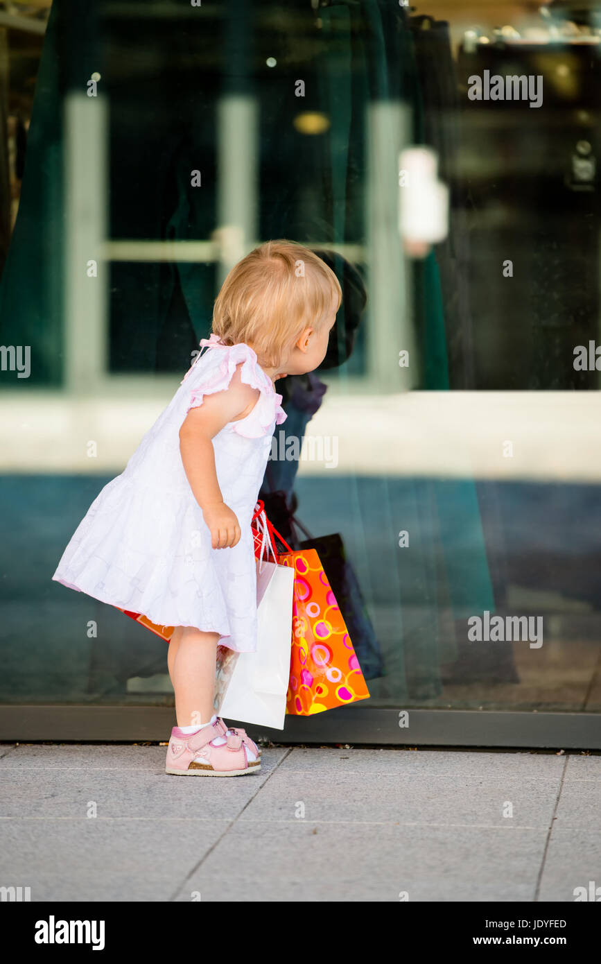 Little girl in white dress looking through shop window Stock Photo - Alamy