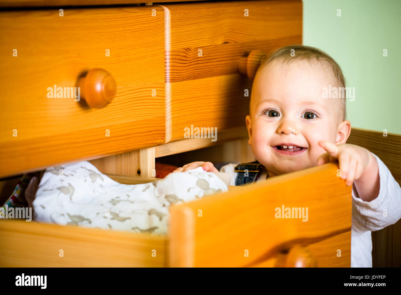 Baby opening drawer with clothes on wooden furniture at home Stock ...