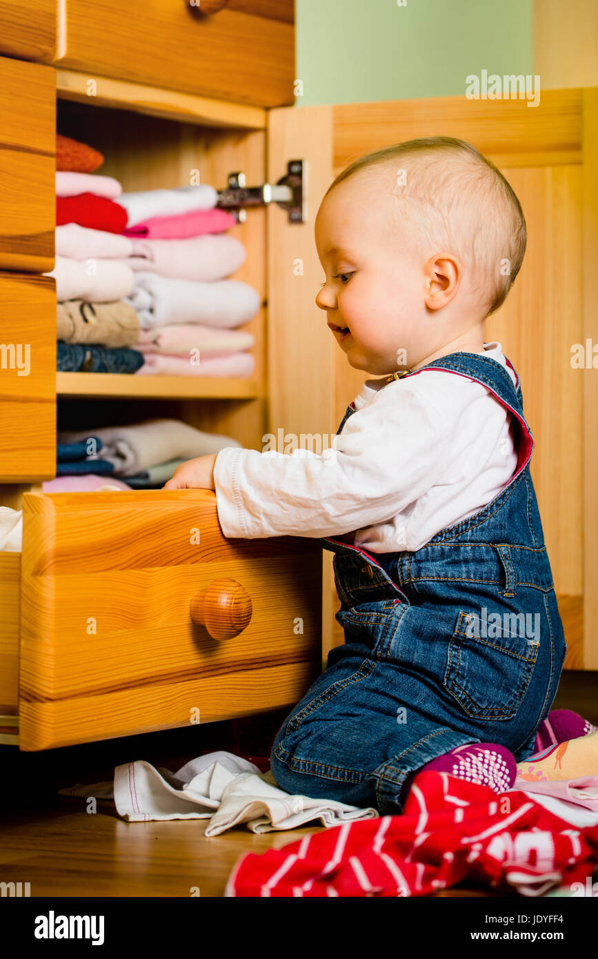 Baby throws out clothes from wooden furniture at home Stock Photo - Alamy
