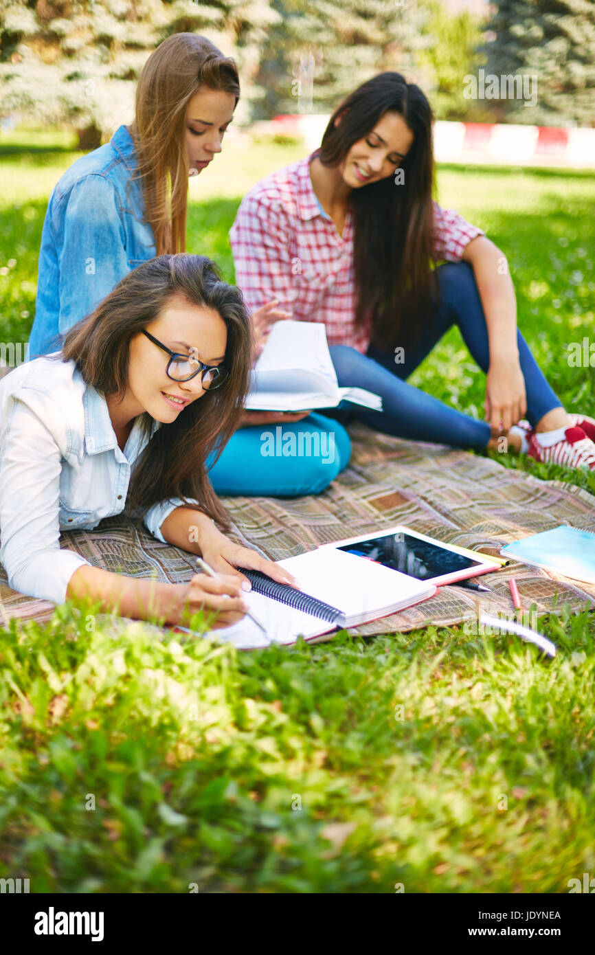 Teenage female making notes in park with her friends on background ...