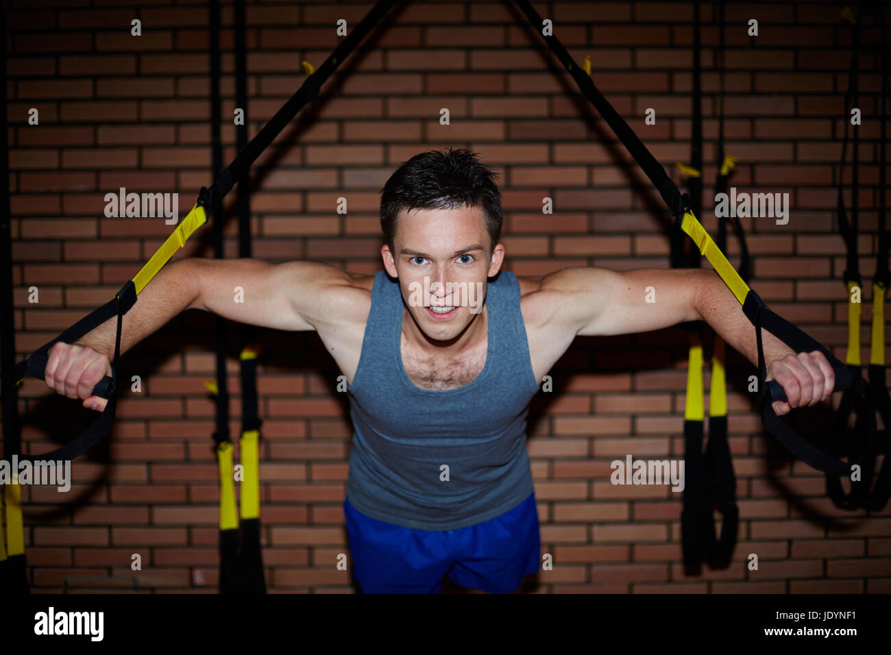 Young man doing exercises for arm muscles over brick wall and looking ...