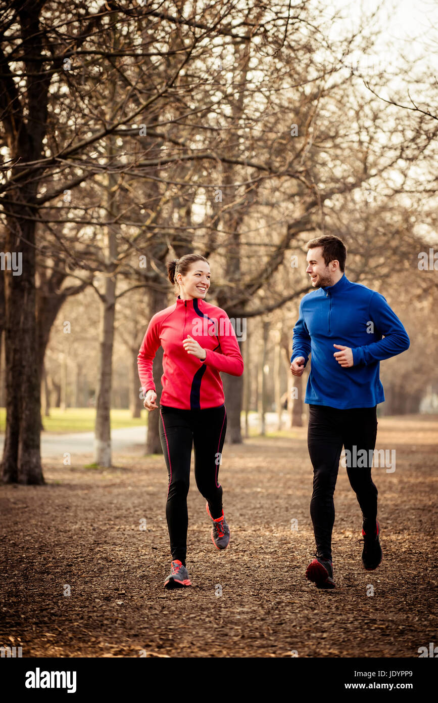 Young couple jogging together in tree alley - looking on each other ...