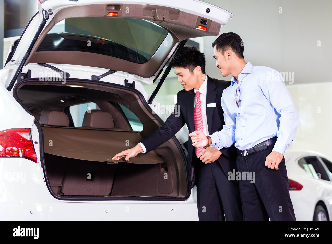 Car salesman in Asian dealership showing trunk of SUV car to customer ...