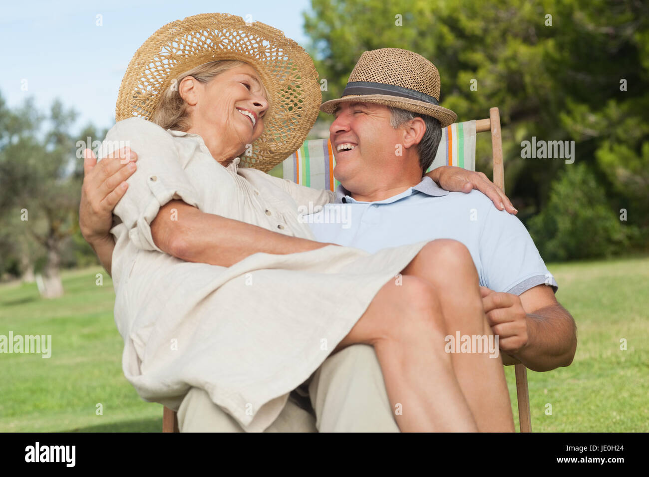 Woman sitting on lap of partner sitting in deck chair and smiling at ...