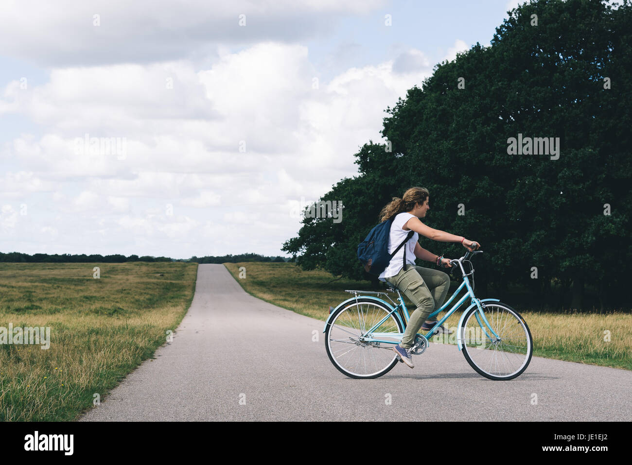 Smiling pretty young woman riding bike in a country road in the park ...