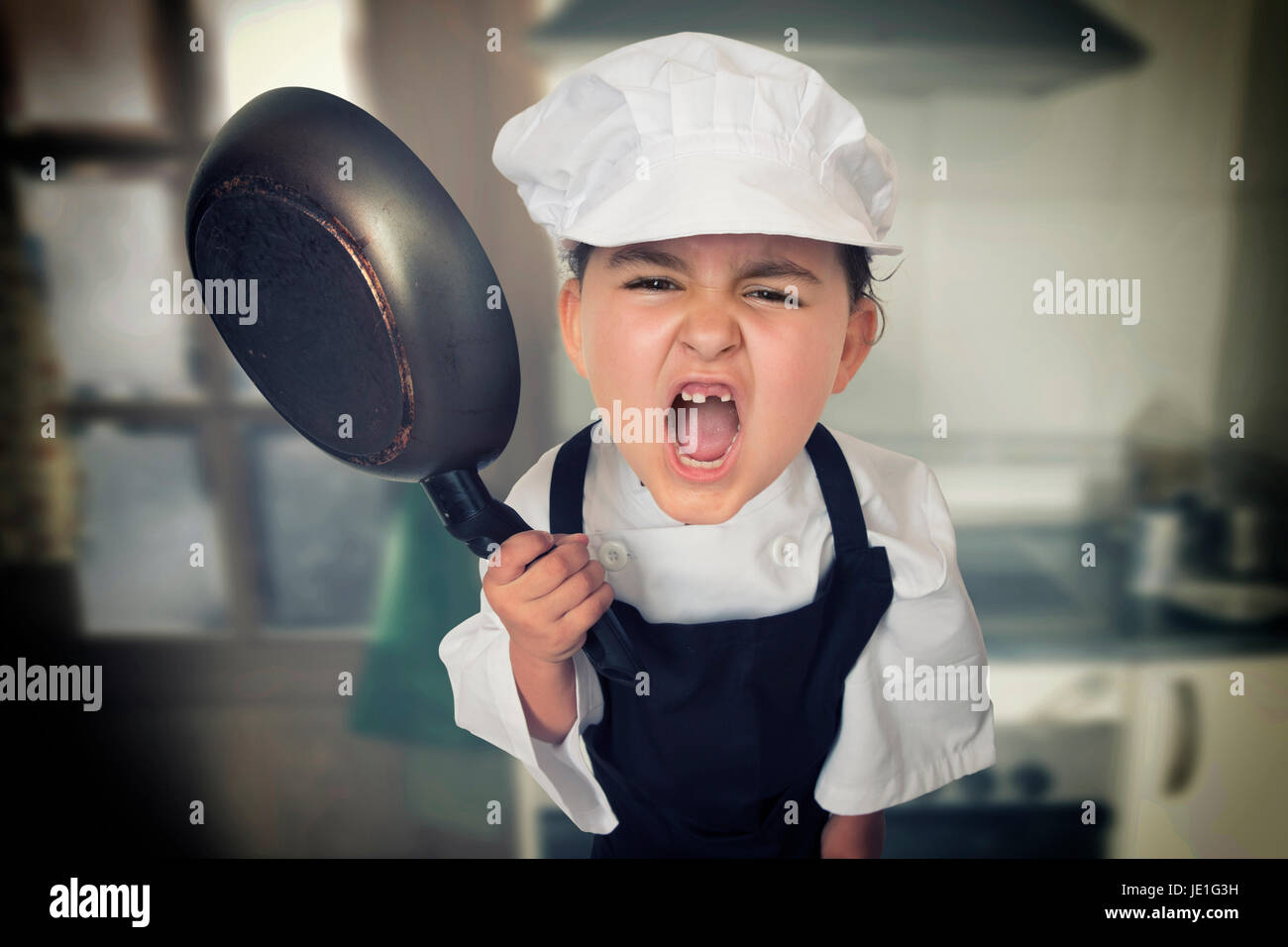 Portrait of a funny six years girl cooking in the kitchen with angry ...