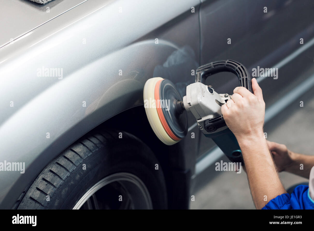 Close-up of hands worker using polisher to polish a gray car body in ...