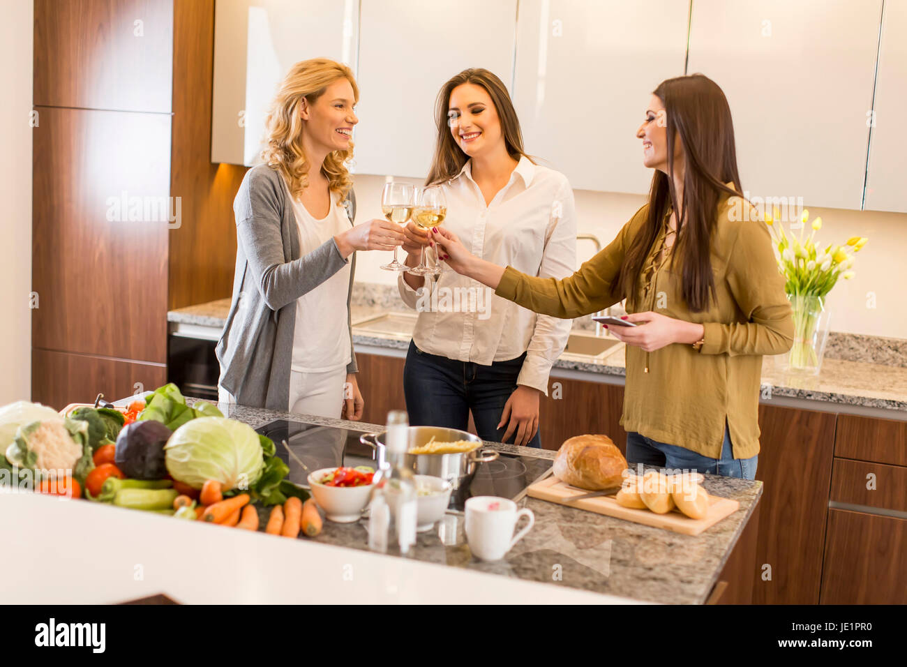 View at three women friends toasting white wine in modern kitchen Stock ...