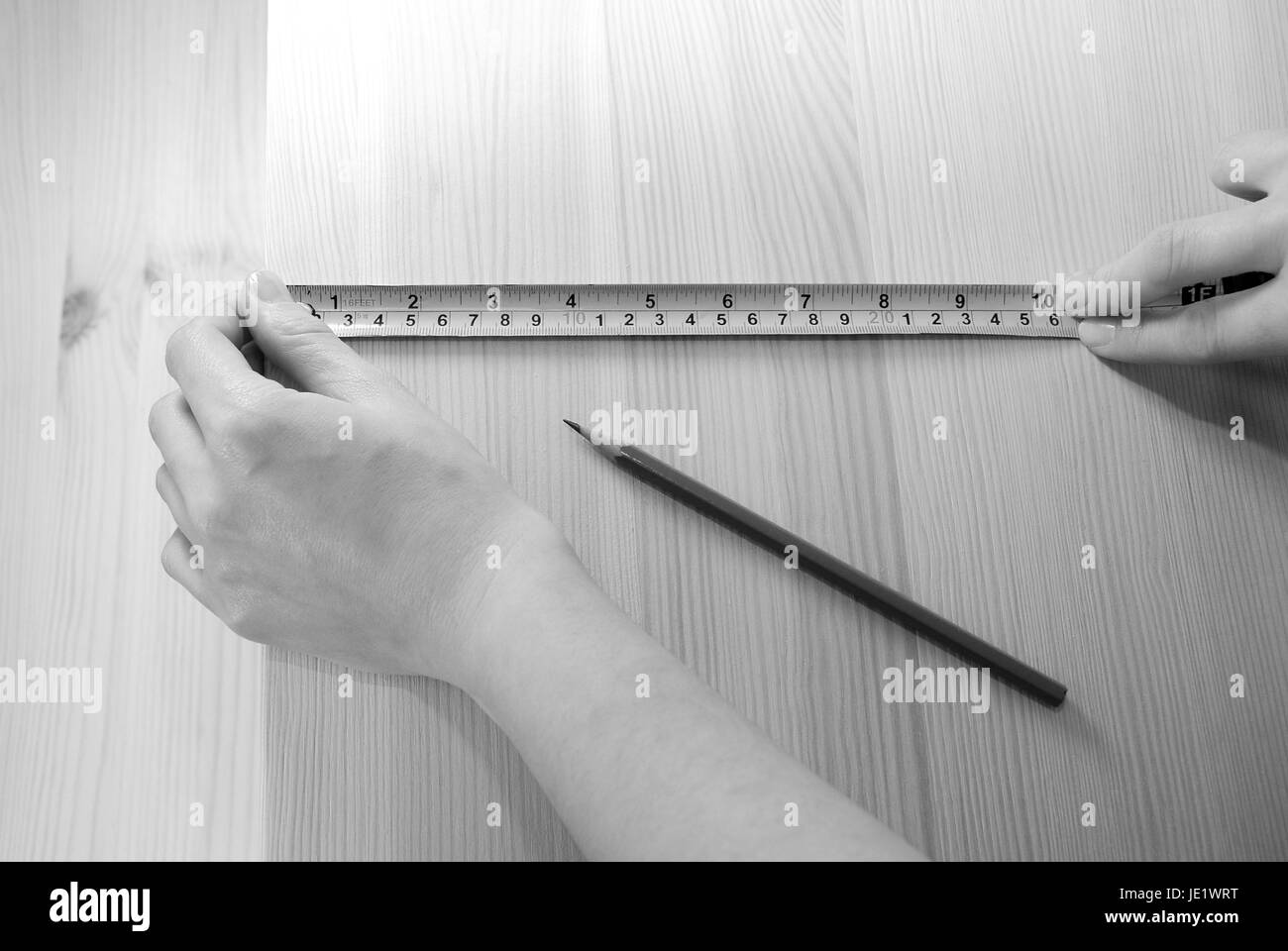 Two hands measuring a wooden board with a steel tape measure in inches ...
