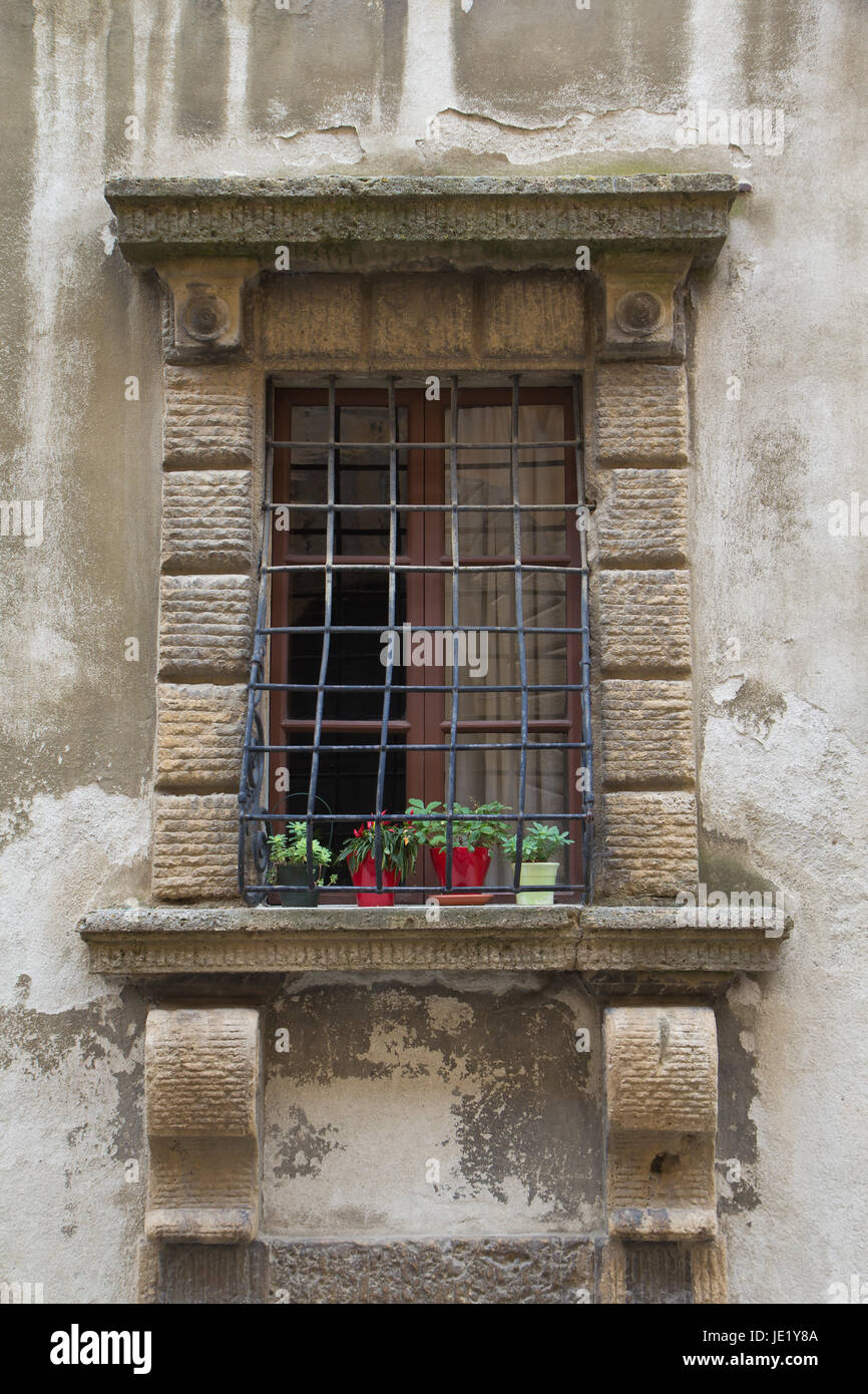 Medieval window with heavy wrought-iron grilles. The plants in red pots ...