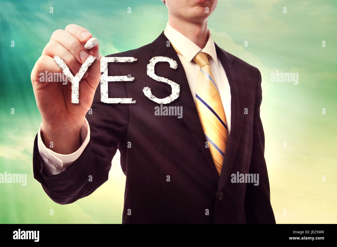 Businessman drawing YES over turquoise yellow colored sky background ...