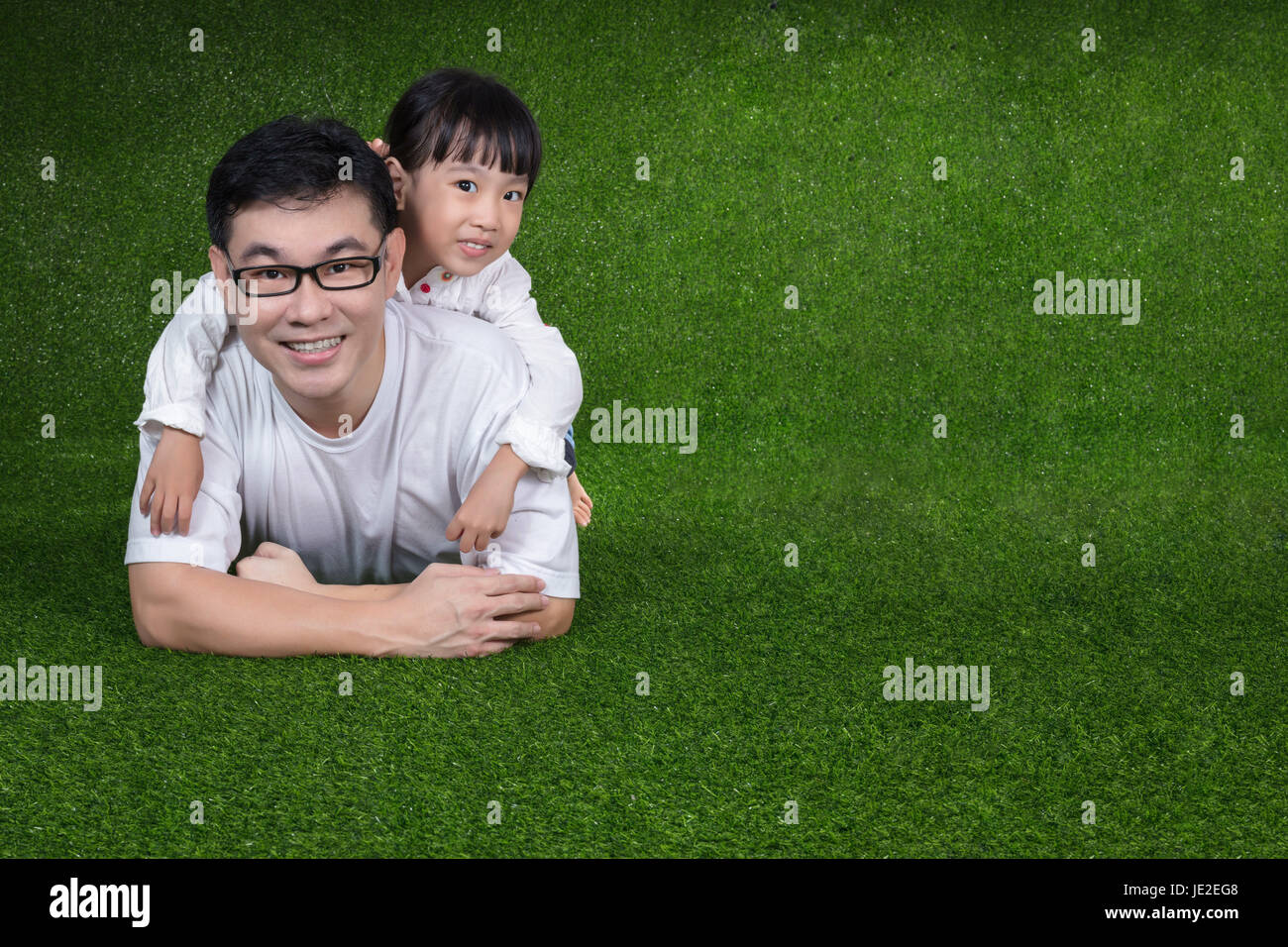 Asian Chinese little girl lying on her father's back at outdoor park ...