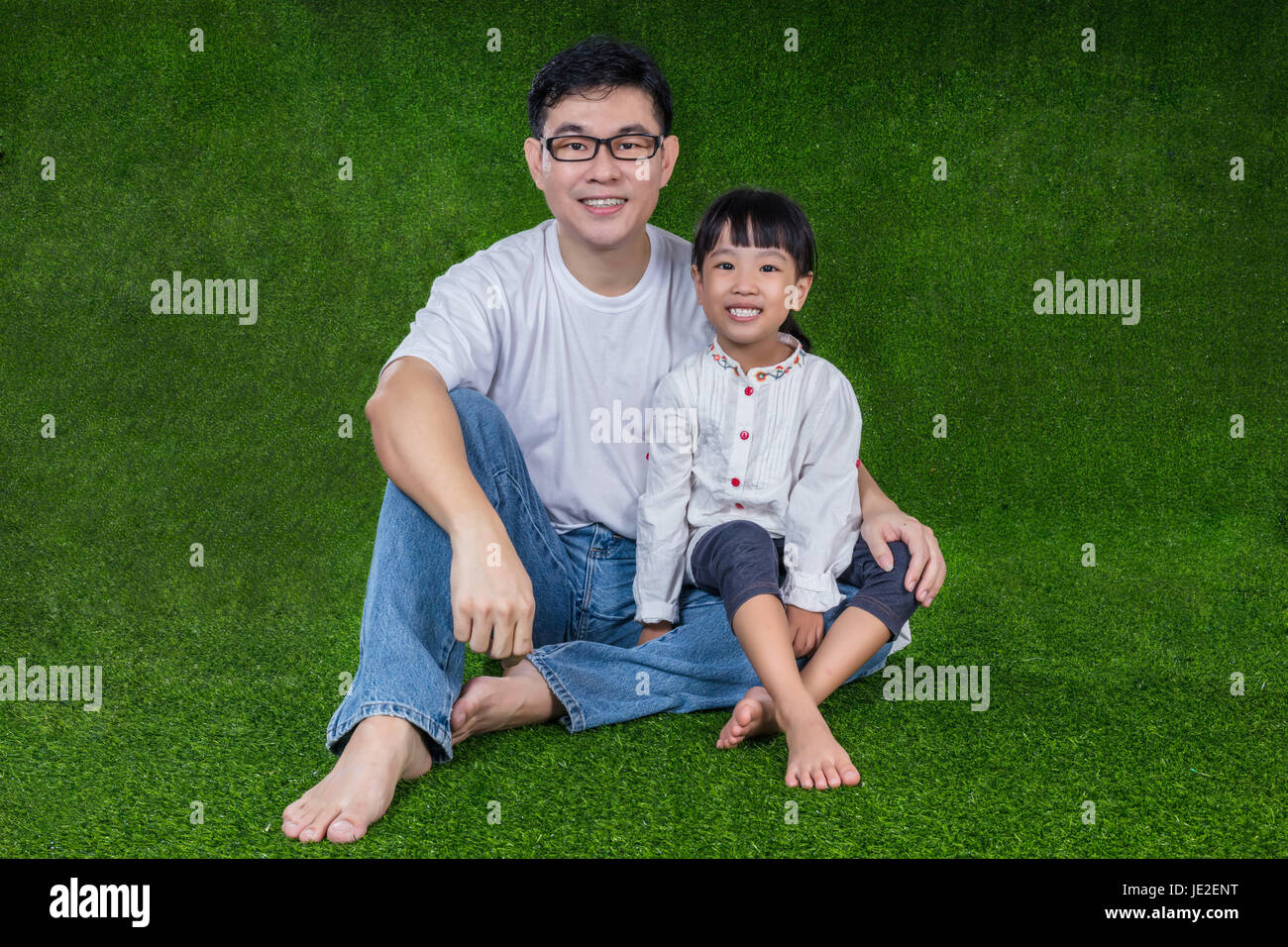 Asian Chinese father and daughter sitting on the grass at outdoor park ...