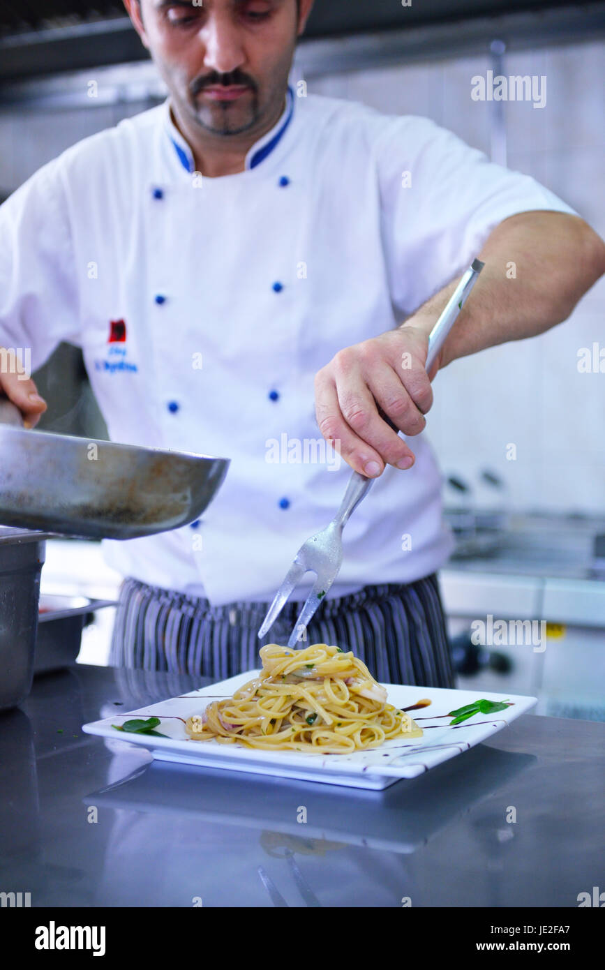 Handsome chef dressed in white uniform decorating pasta salad and ...